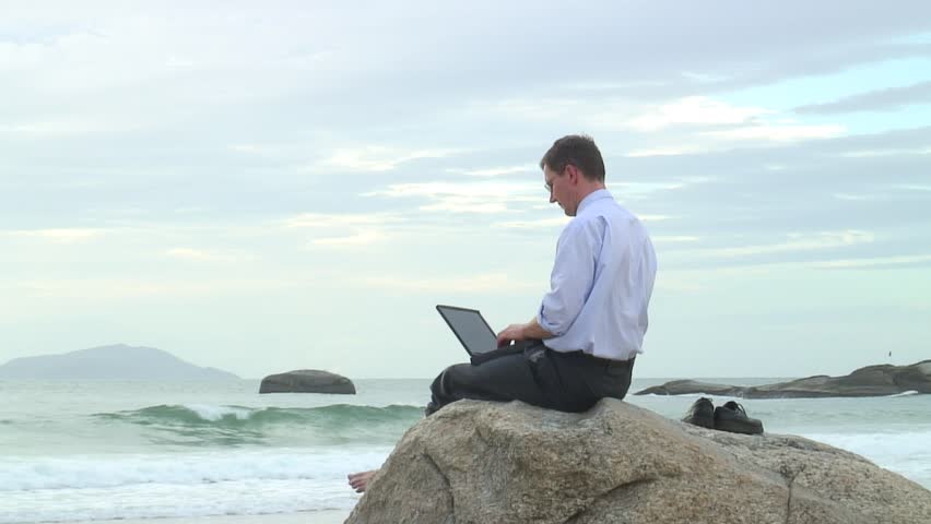 Businessman Working With Laptop While Sitting On A Rock On The Beach ...